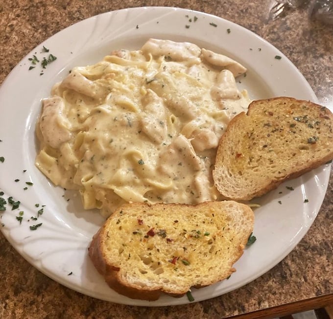 The Alfredo sauce blankets each fettuccine strand like a cozy winter comforter, with garlic bread standing by for sauce-sopping duty.
