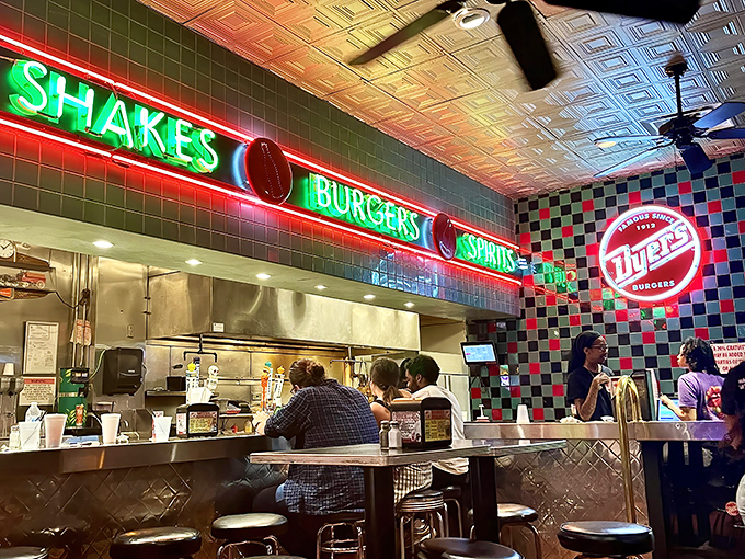 The neon glow above the grill promises three essential food groups: shakes, burgers, and spirits. The holy trinity of diner delights.