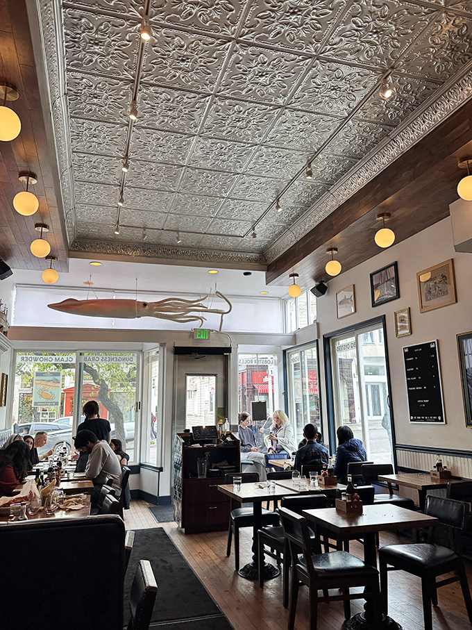 Sunlight streams through large windows, illuminating happy diners and the suspended squid that watches over this seafood sanctuary like a benevolent guardian.