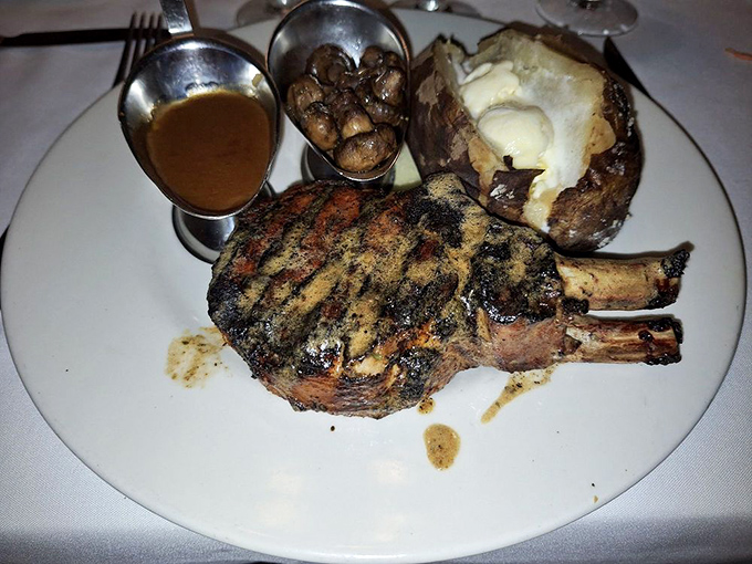 A bone-in pork chop so impressive it deserves its own ZIP code, accompanied by a loaded baked potato and mysterious mushrooms hiding in their silver cave.