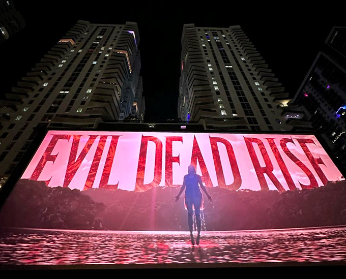 Horror hits differently when watched collectively under open skies, with "Evil Dead Rise" casting its eerie glow across captivated faces.