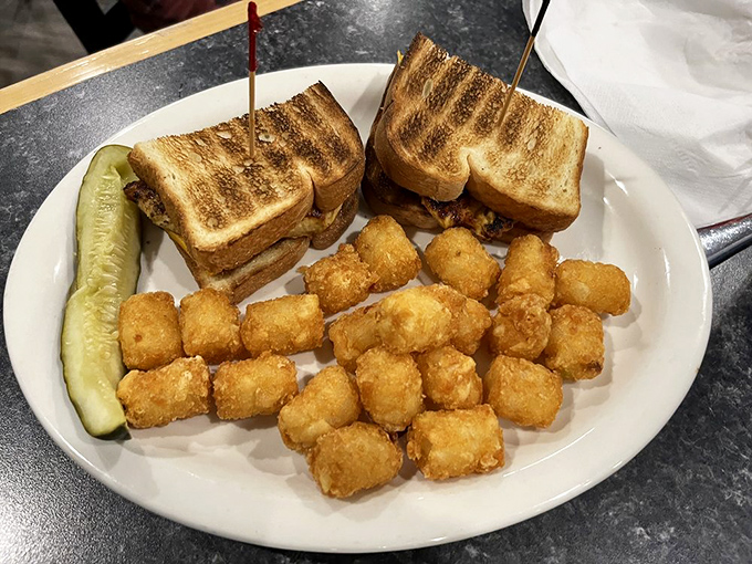 A sandwich that means business, flanked by golden tater tots standing at attention like delicious little soldiers.