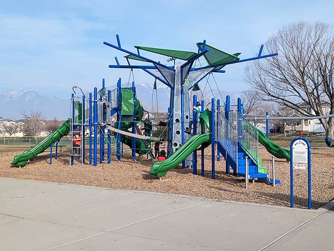 Blue and green playground equipment stands ready for adventure, with mountains in the distance reminding kids that bigger challenges await.