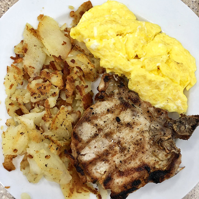The holy trinity of breakfast: perfectly grilled pork chop, sunshine-yellow eggs, and potatoes that have achieved their highest purpose on earth.