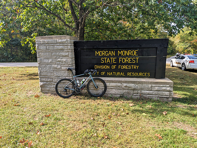 The unassuming entrance sign stands as a portal to adventure, with a cyclist's trusty steed ready for the forest's winding trails.