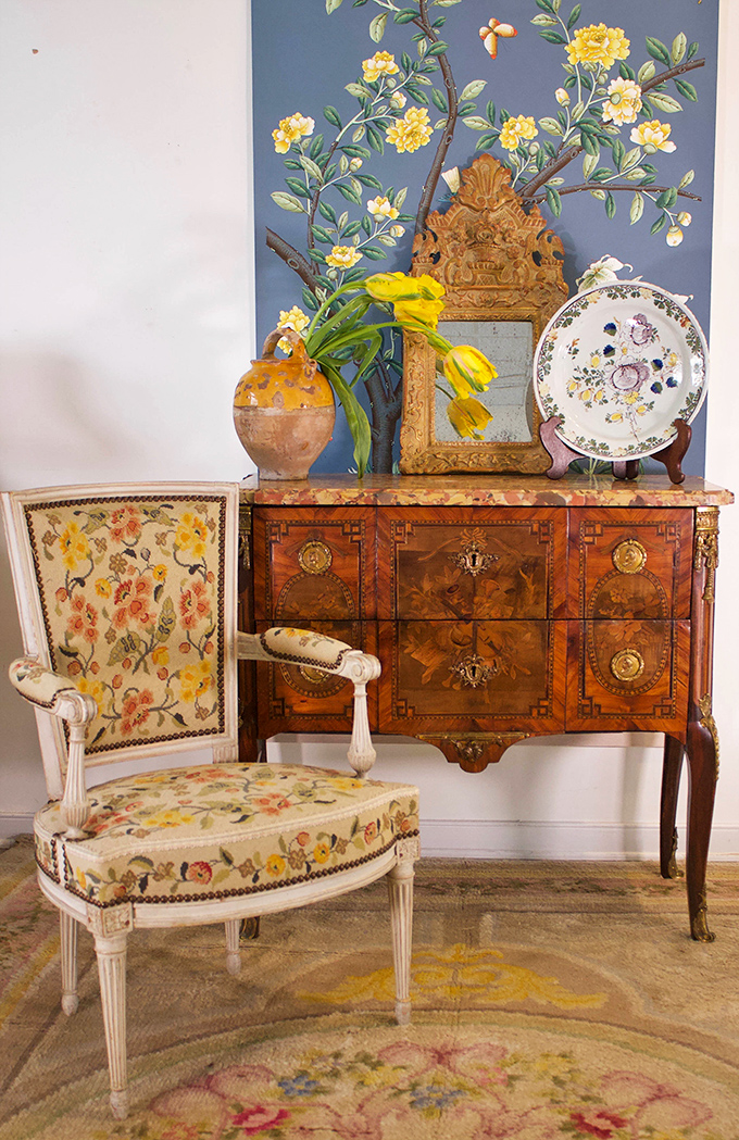 A floral chair that somehow makes botanical upholstery look sophisticated instead of like your grandmother's sofa. That inlaid chest is furniture royalty.