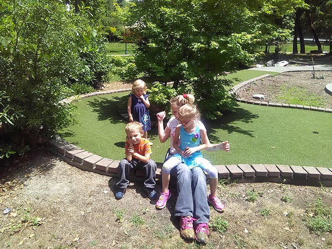 Three young adventurers taking a break from mini-golf – plotting their next move with the serious concentration only childhood allows.