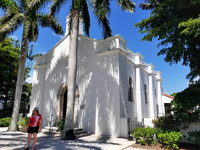 Our Lady of Mercy Catholic Church stands brilliantly white against the blue sky. Palm trees frame this serene spiritual sanctuary.
