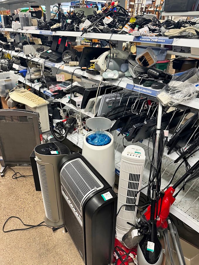 Small appliances and electronics fill shelves like a yard sale crossed with a tech museum from three decades ago.