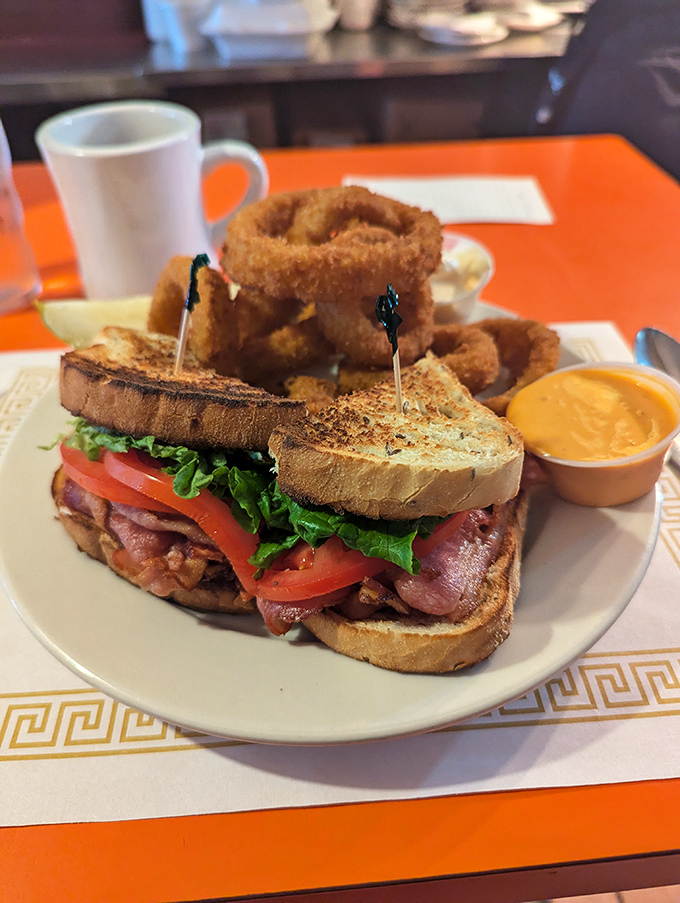 This BLT isn't just a sandwich—it's an architectural masterpiece, flanked by golden onion rings that shatter satisfyingly with each bite.