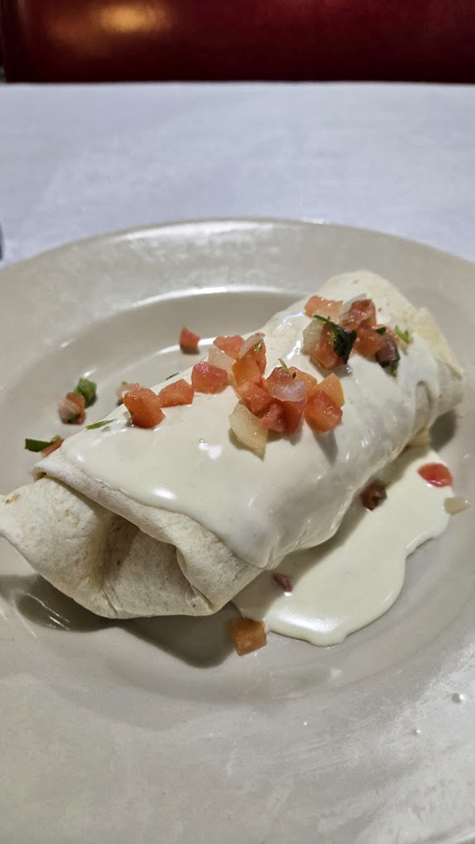 A breakfast burrito wearing a white blanket of queso and a confetti of fresh tomatoes. Morning fuel that's worth setting an alarm for.