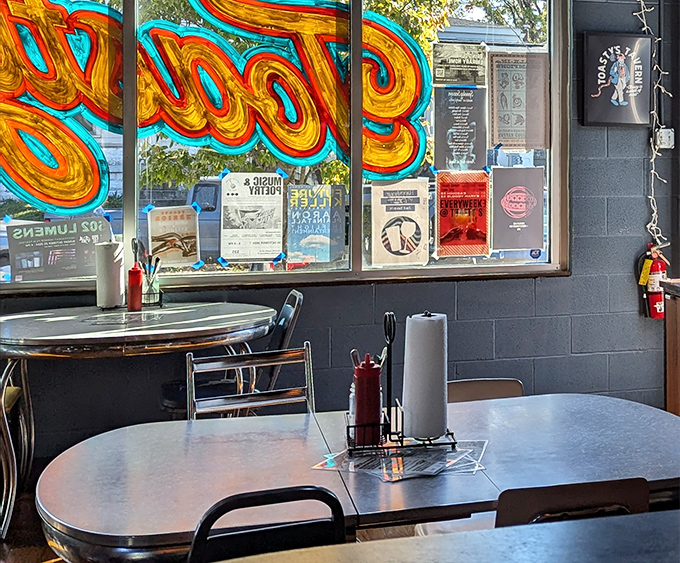 Retro diner tables meet modern tavern vibes. The neon glow through the window reminds you that sometimes the best dining experiences happen in places that don't take themselves too seriously.