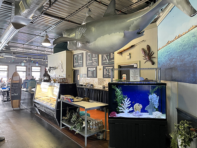 A suspended shark watches over diners like Neptune's guardian while the seafood display case below showcases the day's fresh catches.