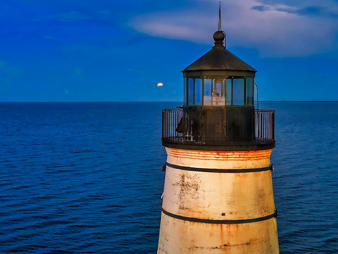 The moon makes a guest appearance alongside the lighthouse, two beacons sharing the night sky in a celestial duet.