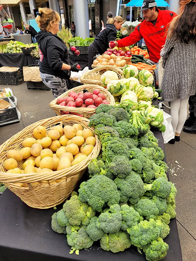 Nature's perfect sculptures. Broccoli crowns and potatoes nestle in wicker baskets while shoppers and vendors engage in the ancient dance of produce selection.