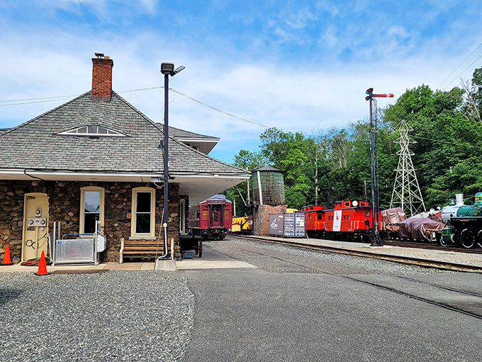 A classic stone station building stands guard while colorful cabooses and vintage equipment create a rainbow of railroad history in the background.