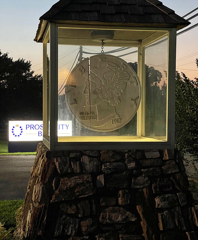 Night brings a golden glow to the giant dime, transforming this roadside curiosity into something almost magical against the twilight sky.