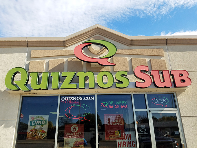 Quiznos' distinctive red and green logo stands out against the beige building. Those toasted subs are calling your name!