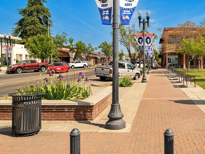 Porterville's charming downtown features brick walkways, military tribute banners, and purple iris flowers blooming in well-maintained planters.