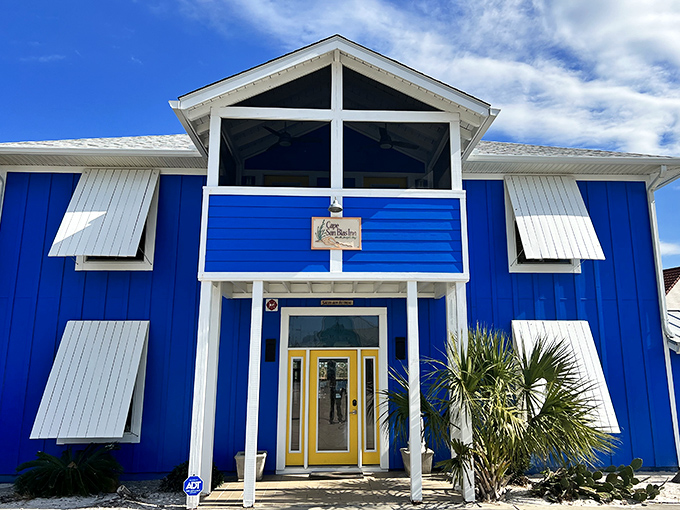 The vibrant blue Cape San Blas Inn pops against the sky, offering a cheerful "howdy" with its sunny yellow door and hurricane shutters ready for whatever comes.