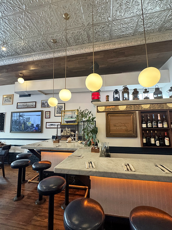 The counter seating offers front-row views of culinary magic, with nautical lanterns and maritime artifacts creating an atmosphere of seafaring sophistication.
