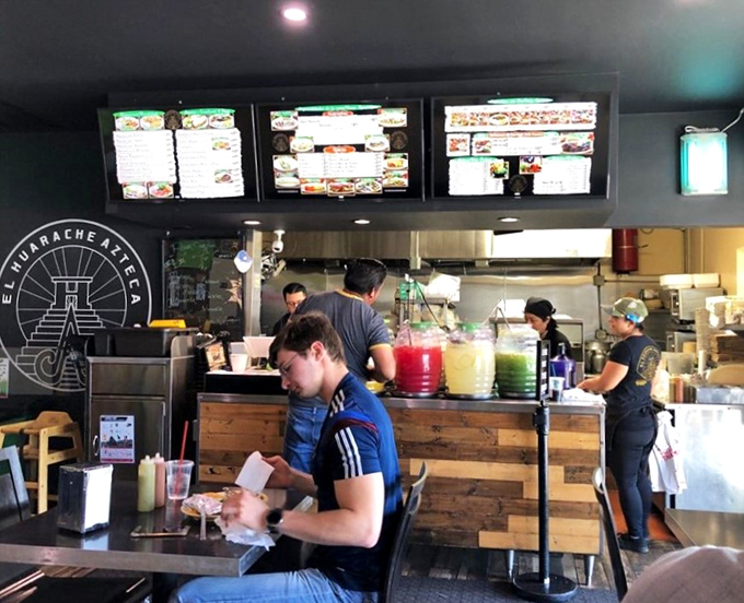 The bustling counter area where colorful aguas frescas tempt from large dispensers while staff efficiently orchestrate the culinary ballet.
