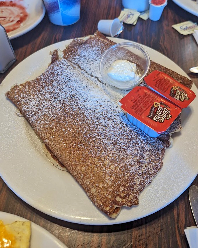 This Danish pancake, dusted with powdered sugar and served with whipped cream, is what breakfast dreams are made of—thin, delicate, and utterly irresistible.