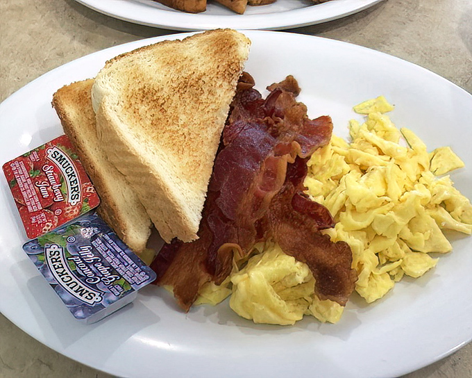 The breakfast trinity: golden toast, perfectly scrambled eggs, and bacon that's achieved that magical balance between crisp and chewy. Morning salvation on a white plate.