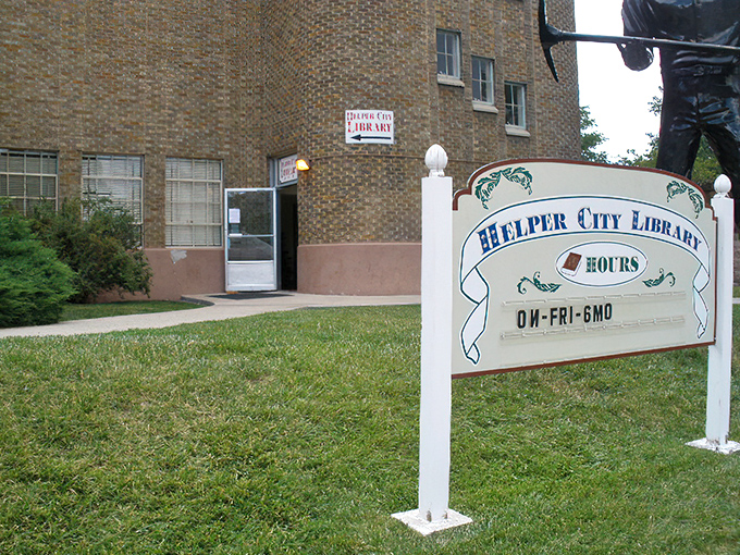 The Helper City Library sign promises books until 6 PM, but the stories contained within these walls extend far beyond closing time or the building's modest brick exterior.