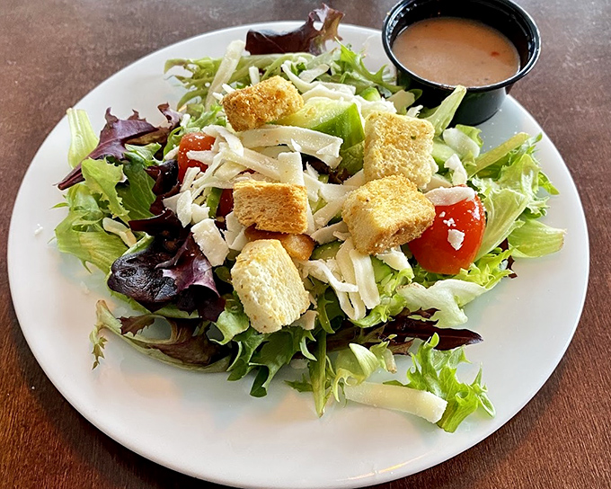 A house salad that actually deserves attention&mdash;crisp greens, golden croutons, and shaved cheese waiting for that house-made dressing shower.
