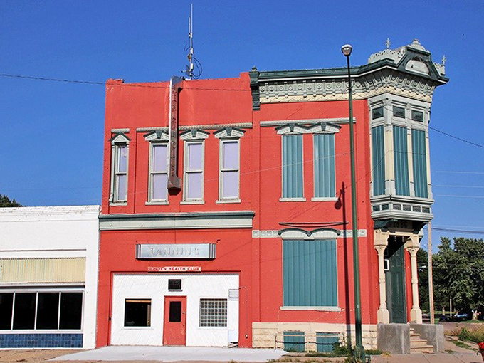 This vibrant red building with its distinctive corner entrance stands as a colorful reminder that small-town architecture often hid big-city ambitions behind those ornate facades. 