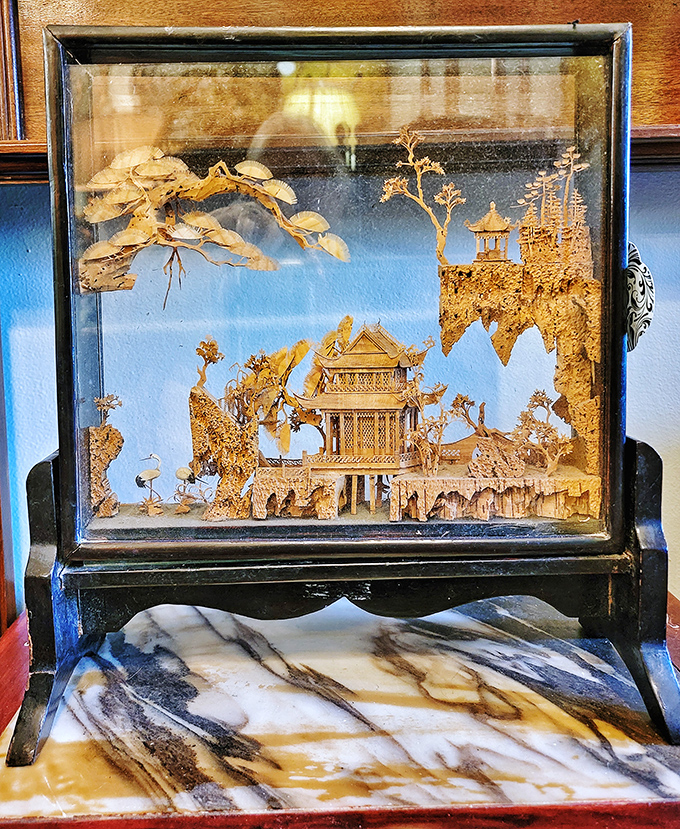 A delicate cork sculpture showcasing Asian architecture sits like a dream captured behind glass, impossibly intricate and hauntingly beautiful.