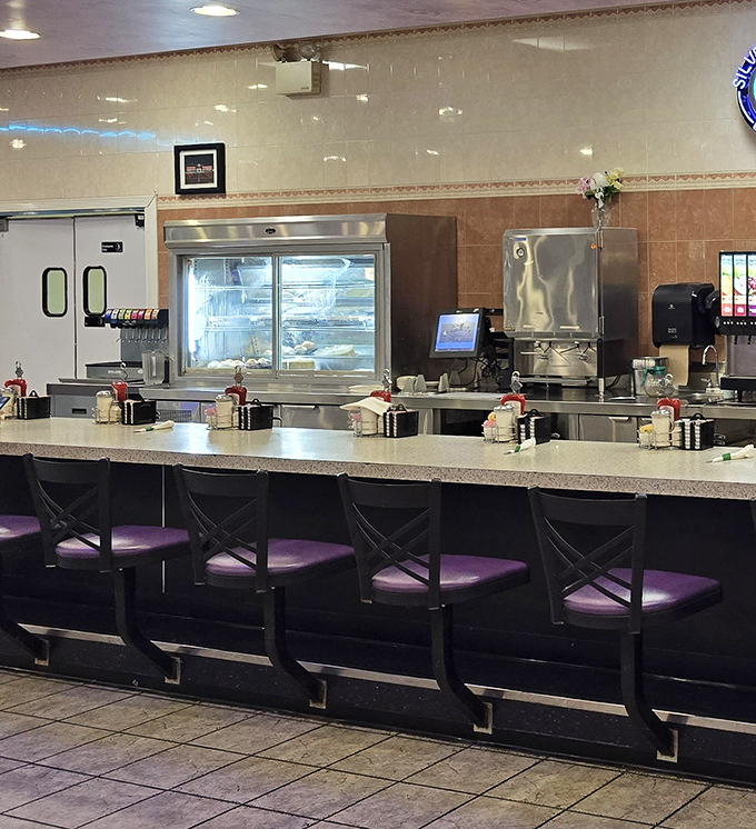 The counter view&mdash;where diner magic happens. Gleaming surfaces, dessert case temptations, and purple chairs awaiting the next hungry customer.