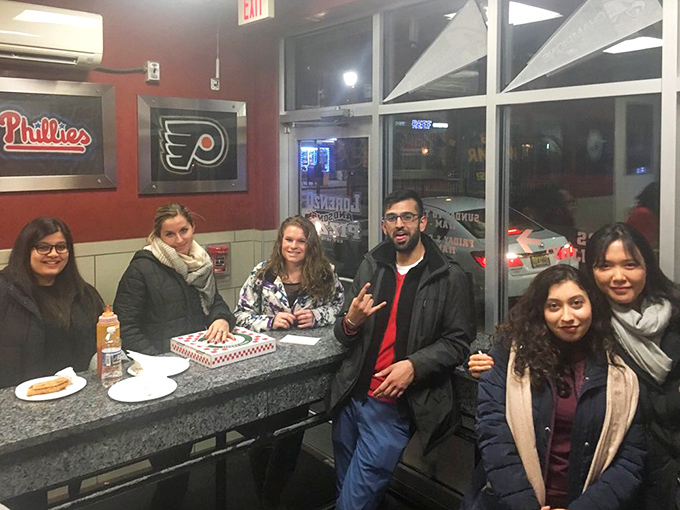Late-night pizza pilgrims gather at the counter, united in their quest for the perfect post-bar slice.