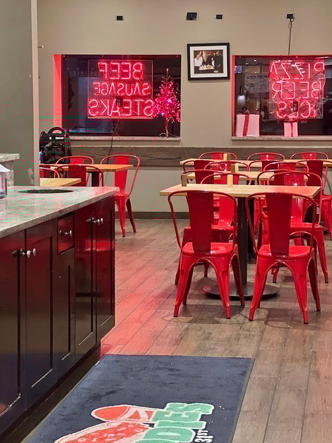 Red chairs pop against neutral walls like exclamation points in a love letter to Italian-American food. The neon signs glow with promises they fully intend to keep.