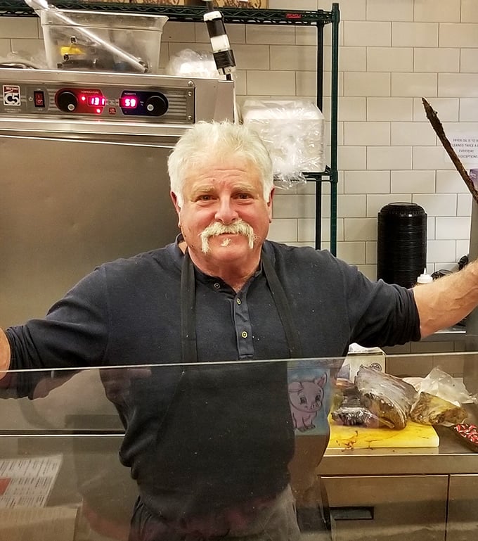 The image shows what appears to be a staff member in the kitchen area, embodying the hands-on dedication that transforms raw ingredients into BBQ masterpieces.