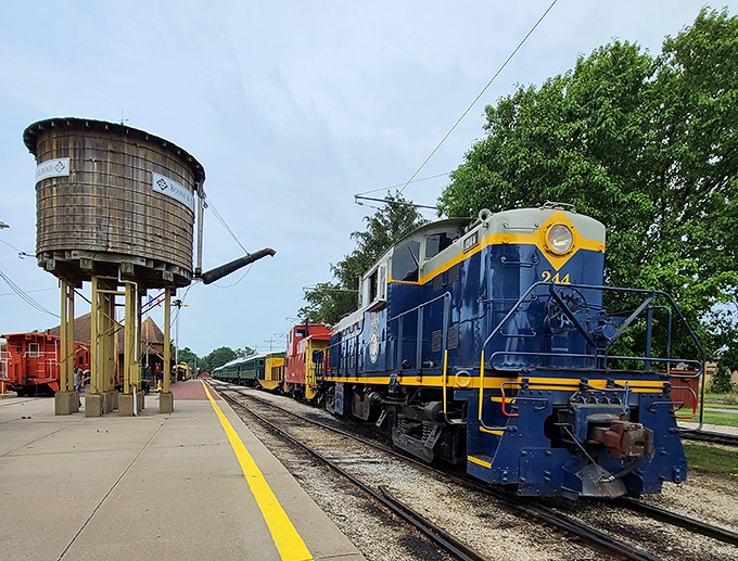 The striking blue and yellow locomotive stands guard beside a wooden water tower, essential infrastructure from steam railroading days.