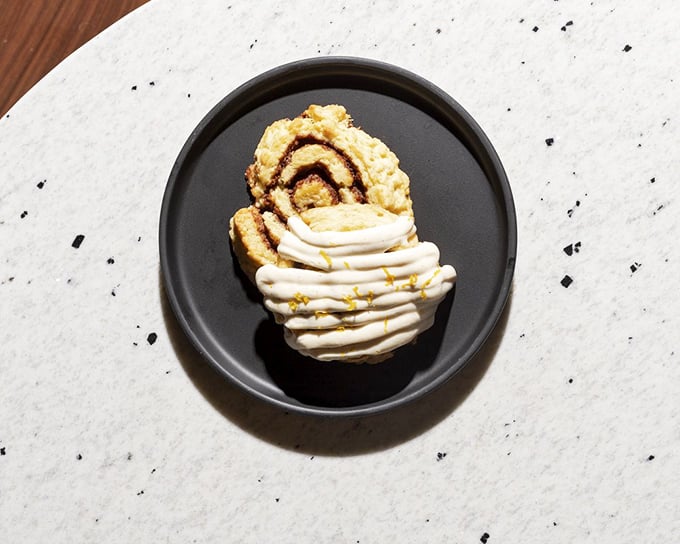 A cinnamon roll reimagined as a scone, topped with a cloud of cream that's melting into sweet surrender on its warm surface.