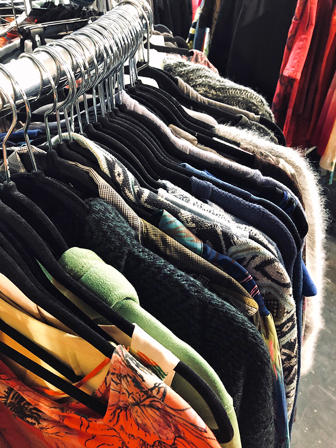 Sweaters and jackets hang like textile tapestries, each pattern and texture telling the story of a different decade's fashion sense.