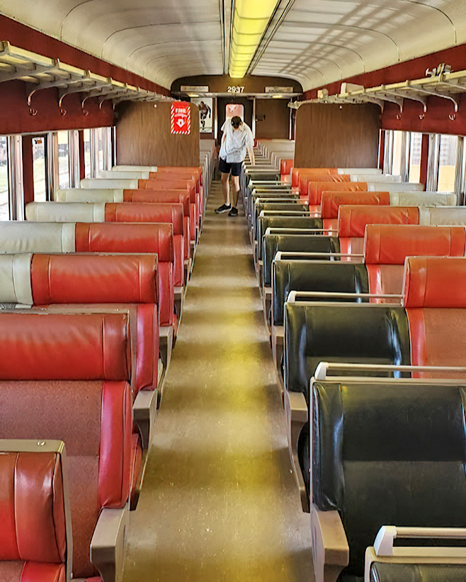 The vintage passenger car interior, with its rows of red and black seats, offers a glimpse into mid-century travel comfort that made train journeys special for millions of Americans.