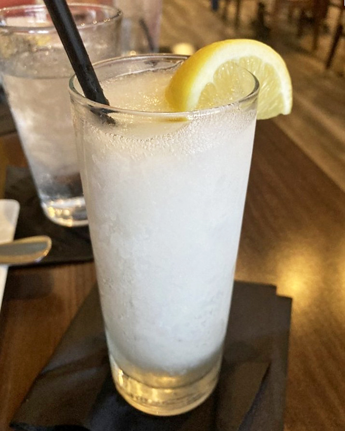 A tall glass of lavender lemonade that's both refreshment and visual poetry. The condensation beads promise relief from seafood's salty embrace.