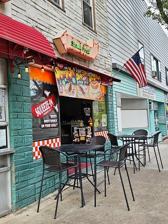 Outdoor seating expands the Squeeze-In experience beyond its namesake confines. The American flag adds a touch of patriotism to this hot dog pilgrimage.