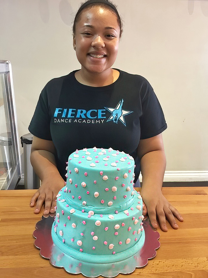 A proud baker with her masterpiece. That turquoise cake with pink and white accents isn't just dessert&mdash;it's someone's celebration waiting to happen.