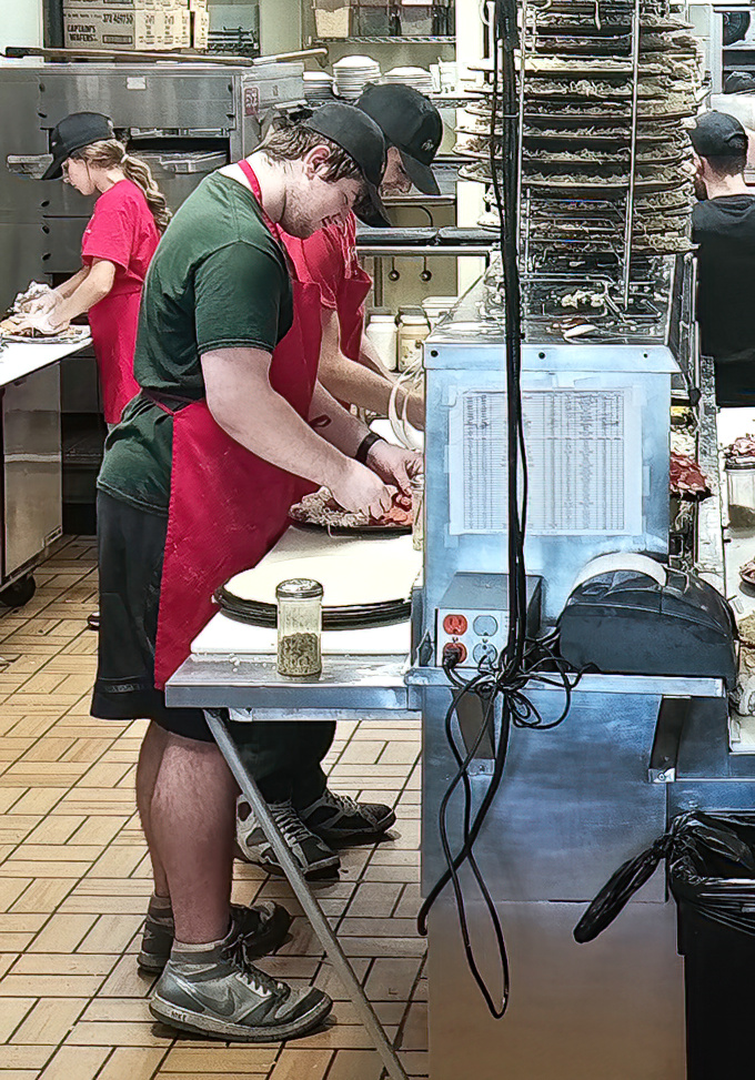 Pizza artisans at work! These skilled hands transform simple ingredients into edible masterpieces that keep locals coming back week after week.