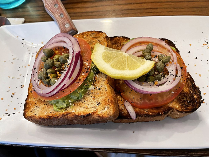 Avocado toast elevated&mdash;thick-cut bread supporting the perfect stack of tomato, red onion, capers, and lemon that makes "trendy" taste timeless.