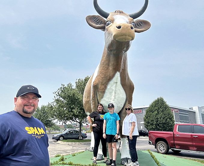 Generations gather at Bessie's hooves, continuing the timeless tradition of saying, "We saw the giant cow!" to disbelieving friends back home.