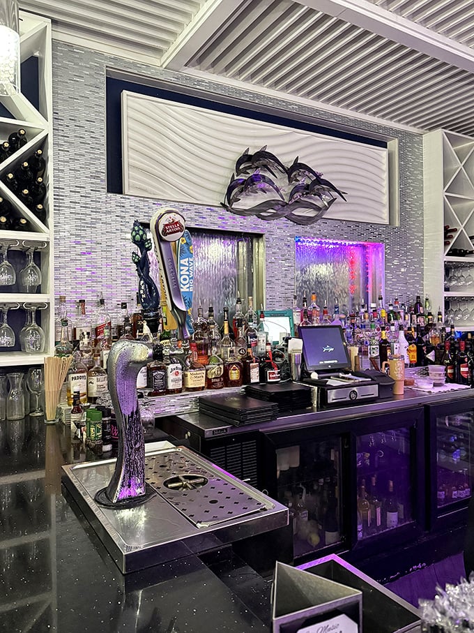 The bar gleams with bottles of promise, while metal dolphins dance overhead—because nothing says "coastal drinking" quite like marine mammals supervising your martini.