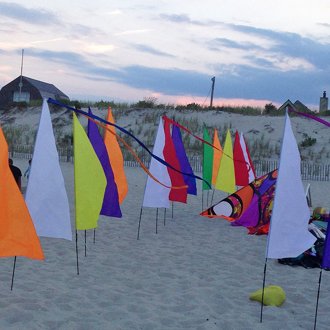Colorful beach flags dance in the evening breeze, a whimsical rainbow against dunes that have stood watch for centuries.