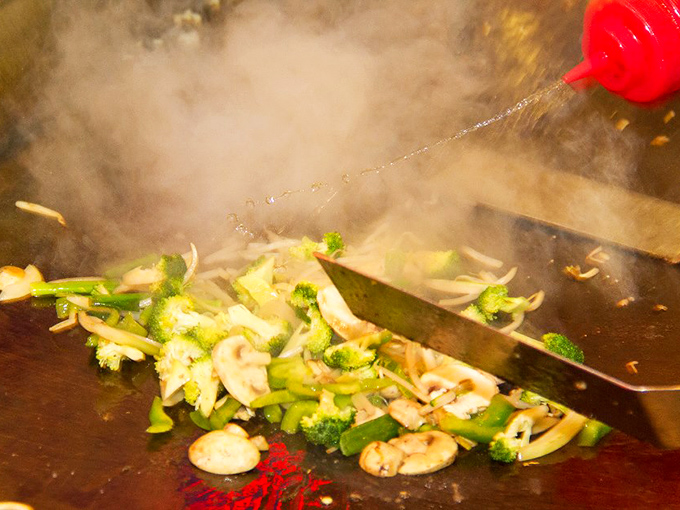 Steam rises like culinary special effects as vegetables meet hot griddle in the ancient hibachi dance of flavor transformation.