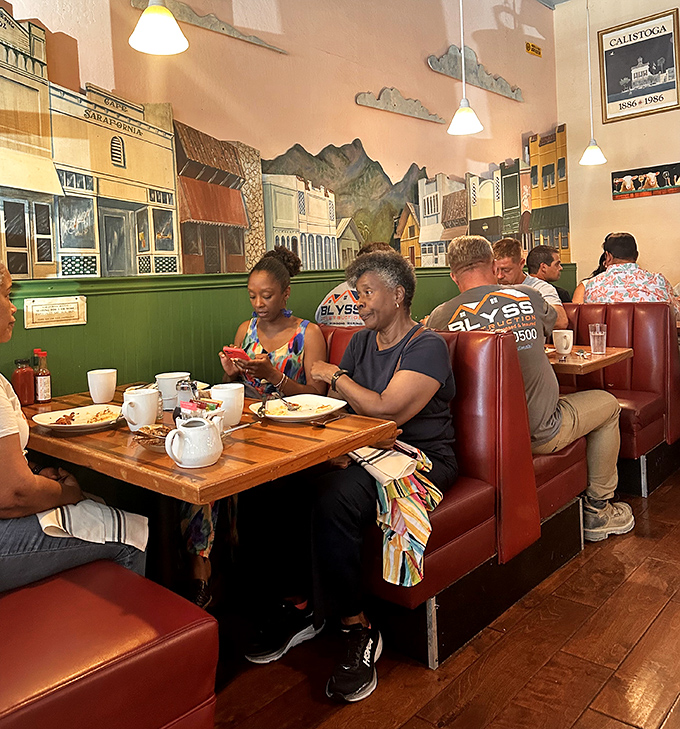 Red booth seating cradles diners as they dive into breakfast feasts, with the historic Calistoga mural providing a sense of place and time.